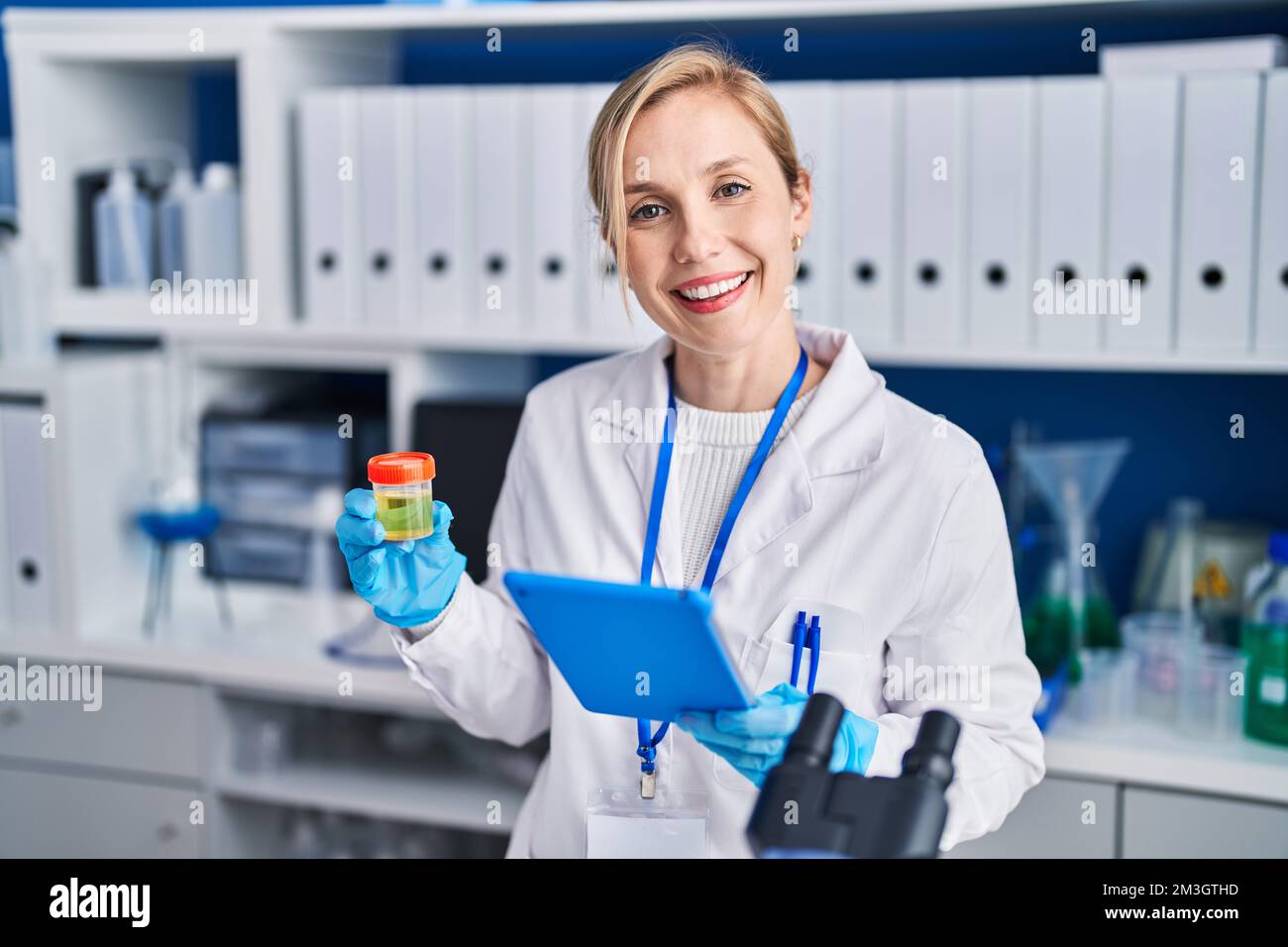 Young blonde woman scientist using touchpad holding urine test tube at ...