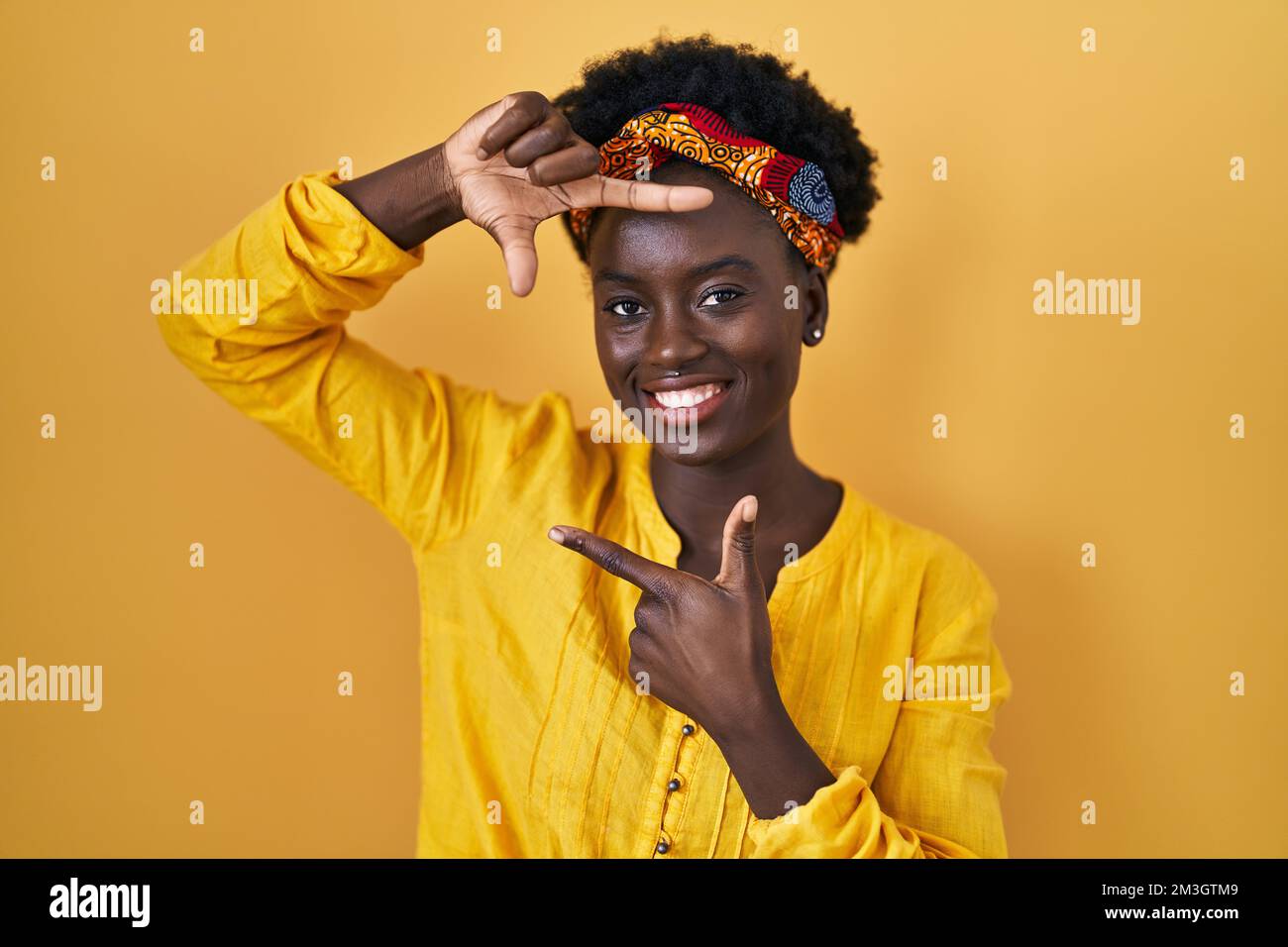 African young woman wearing african turban smiling making frame with ...