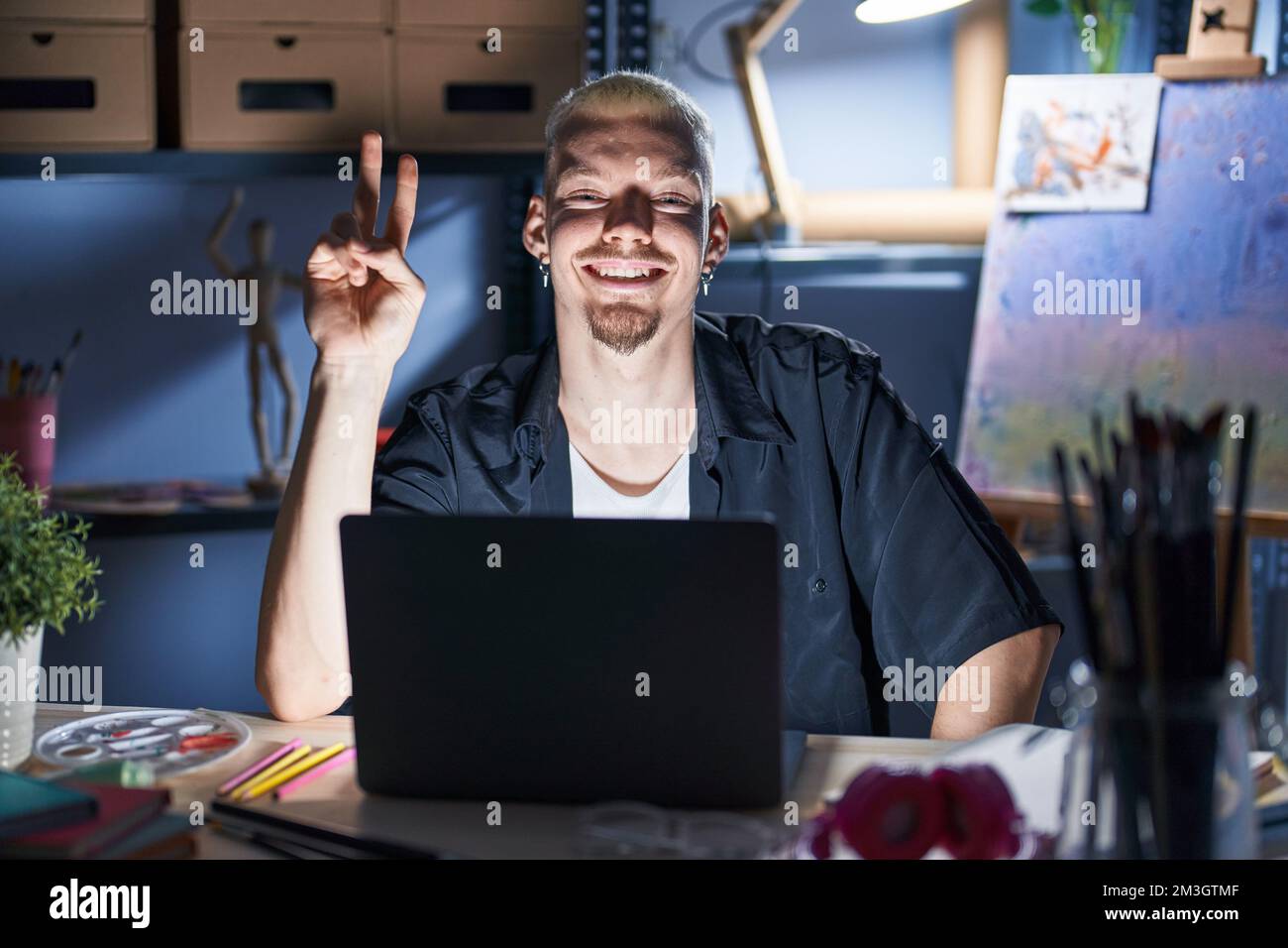 Young caucasian man using laptop at night at art studio showing and ...