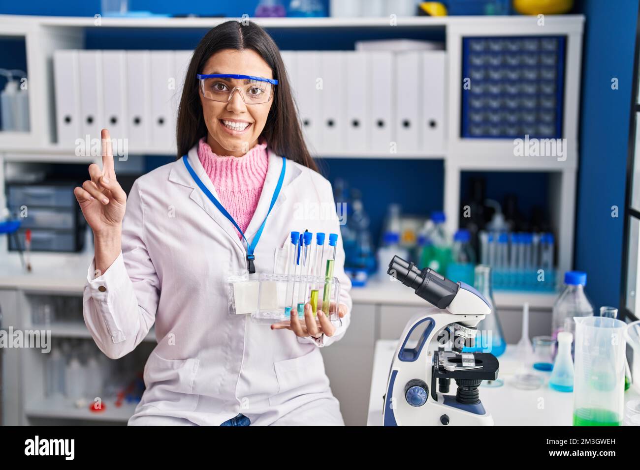 Young brunette woman working at scientist laboratory surprised with an idea or question pointing ...