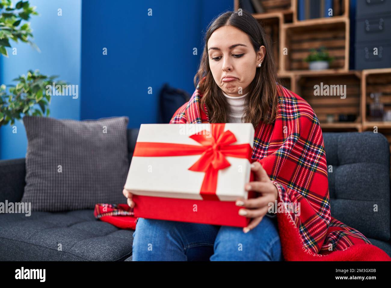 Young hispanic woman opening gift box depressed and worry for distress ...
