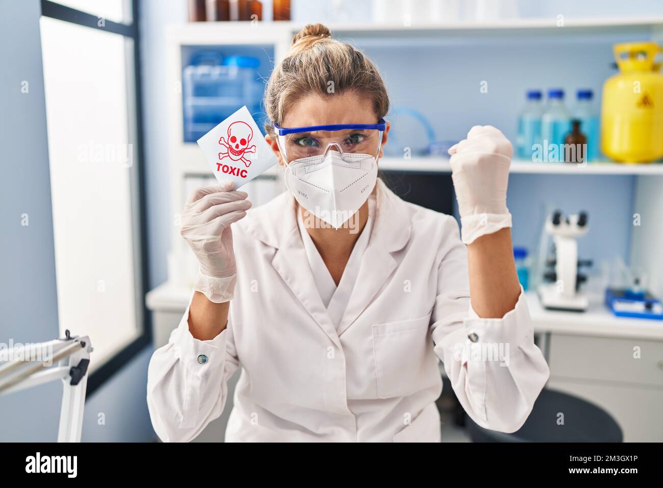 Young woman working at scientist laboratory holding toxic banner ...