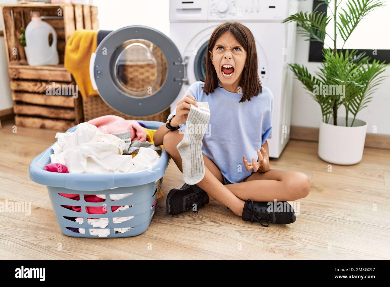 Young hispanic girl doing laundry holding socks angry and mad screaming ...