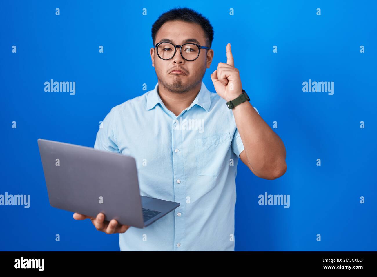 Chinese young man using computer laptop pointing up looking sad and ...