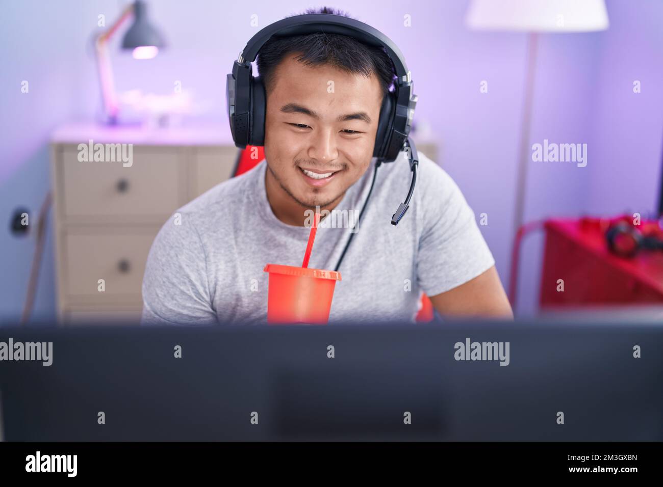 Young chinese man streamer playing video game drinking beverage at ...