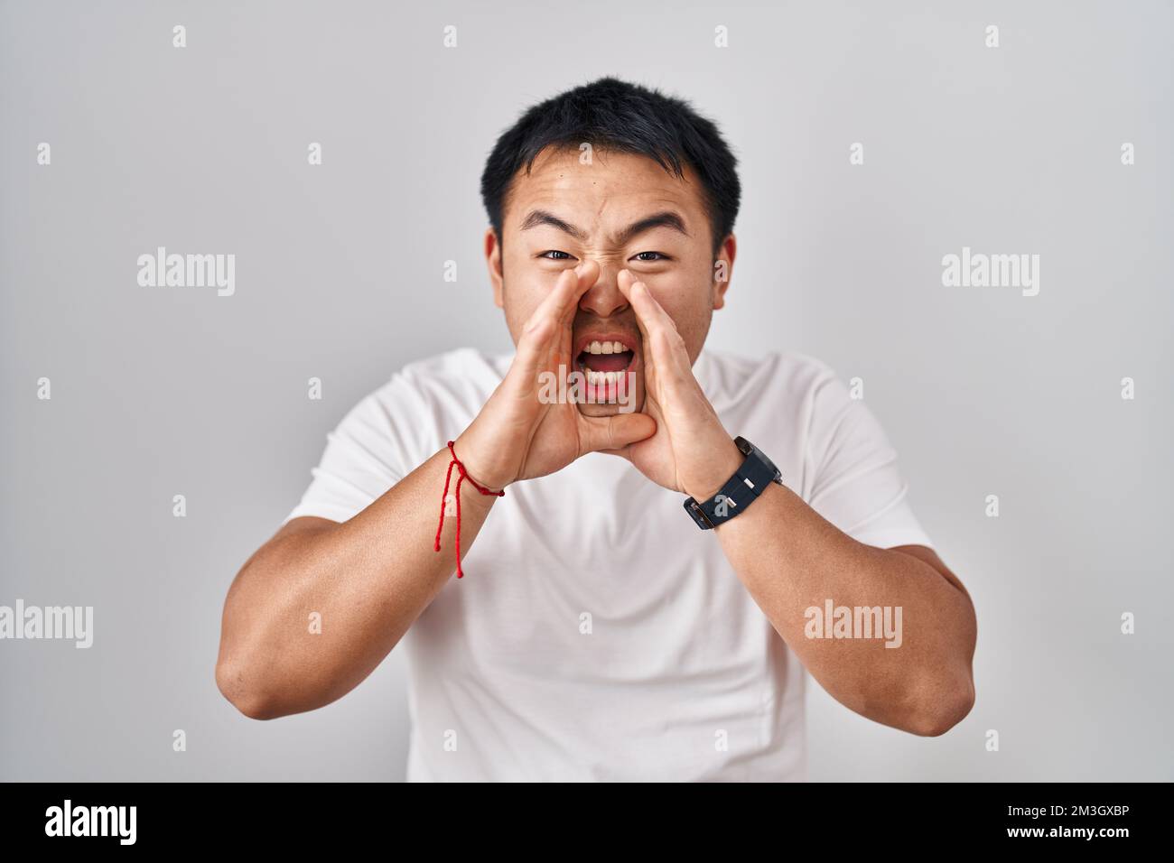 Young chinese man standing over white background shouting angry out ...
