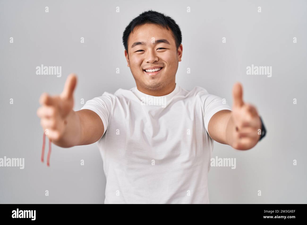 Young chinese man standing over white background looking at the camera ...
