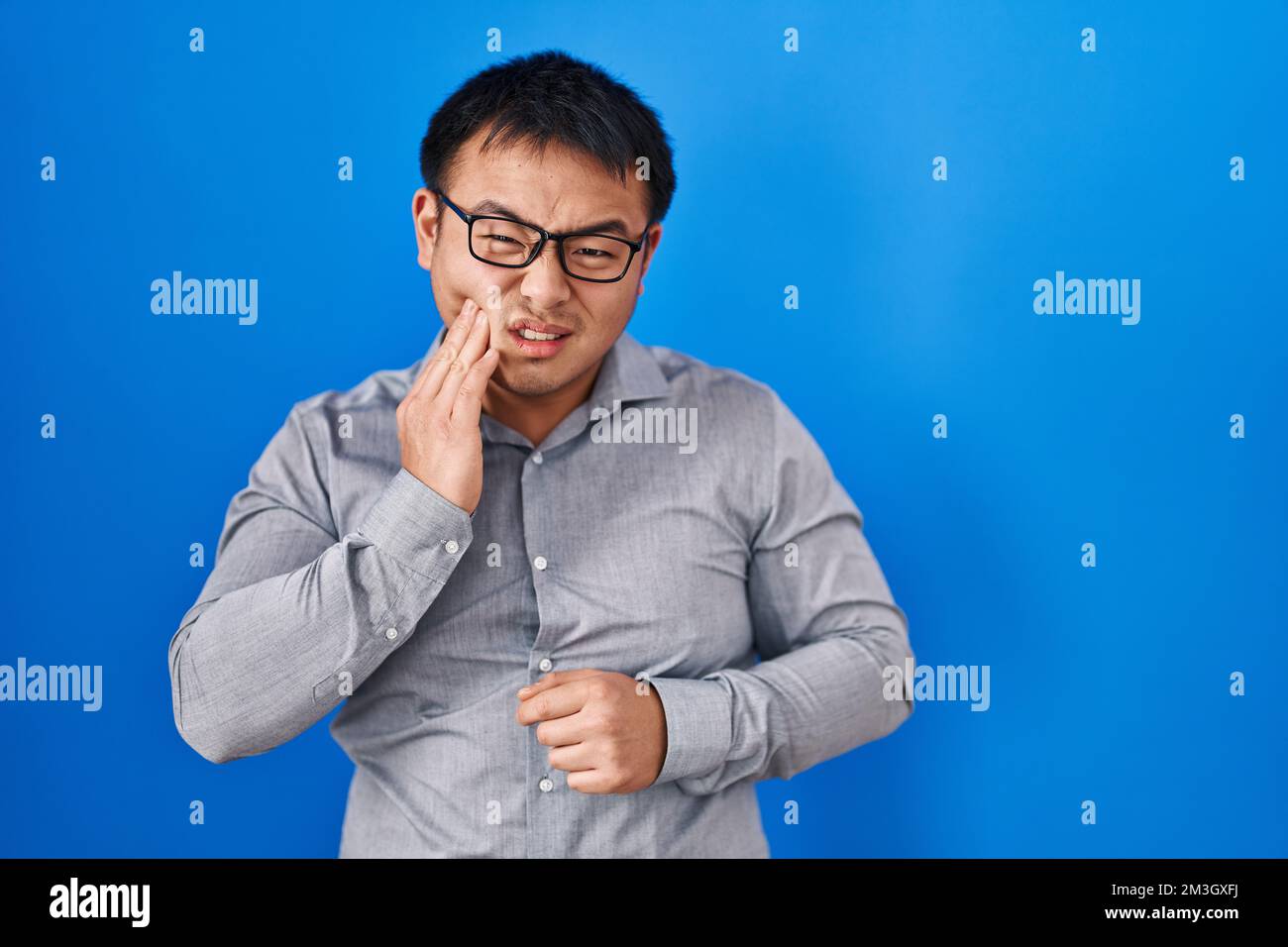 Young chinese man standing over blue background touching mouth with ...