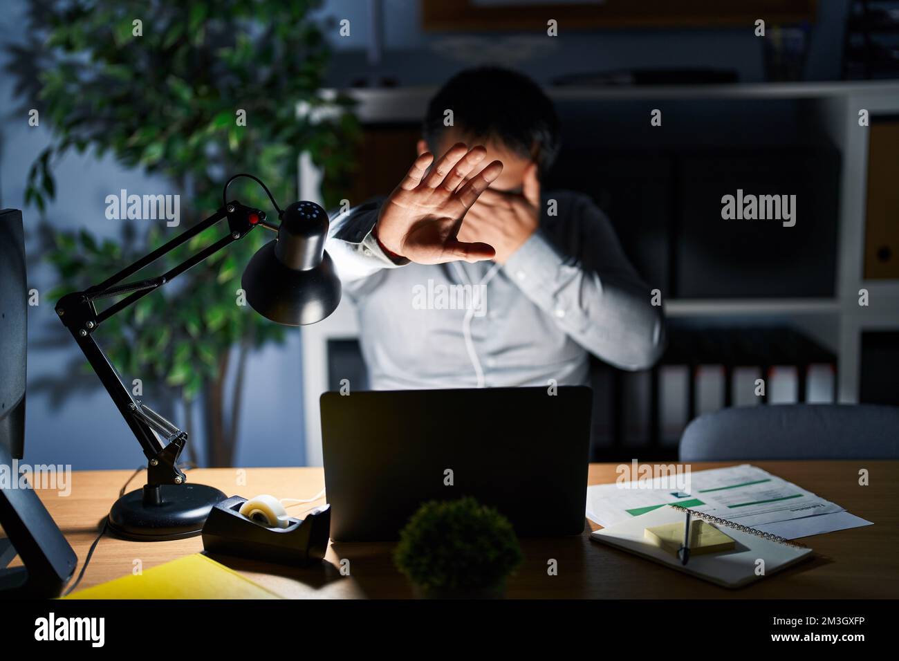 Young chinese man working using computer laptop at night covering eyes ...