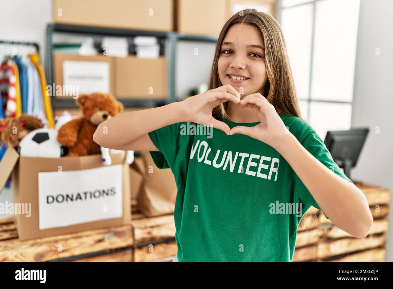 Adorable girl wearing volunteer uniform doing heart symbol with hands ...