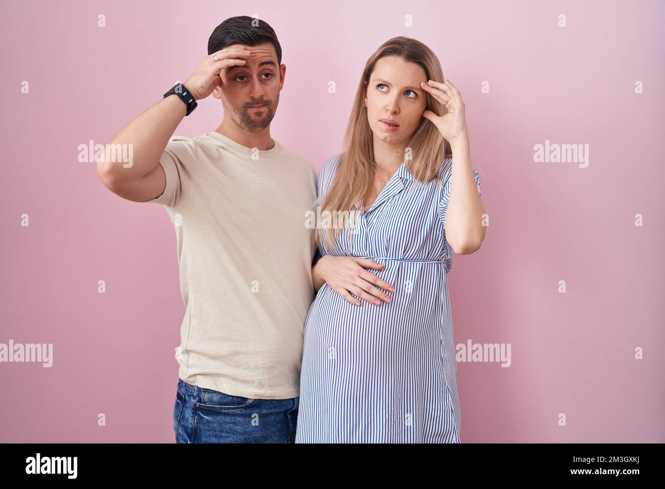 Young couple expecting a baby standing over pink background worried and ...