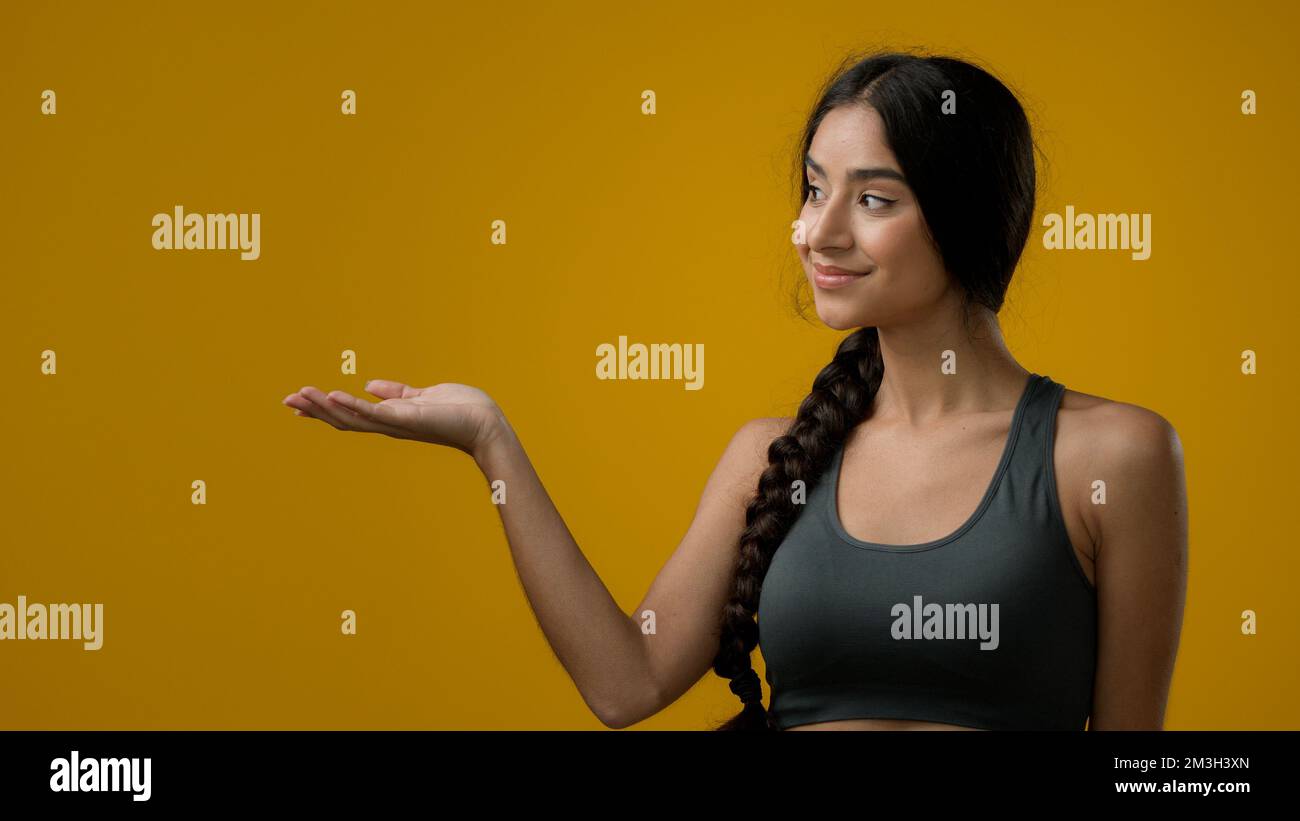 Portrait Indian 20s woman in studio yellow background pointing to side ...