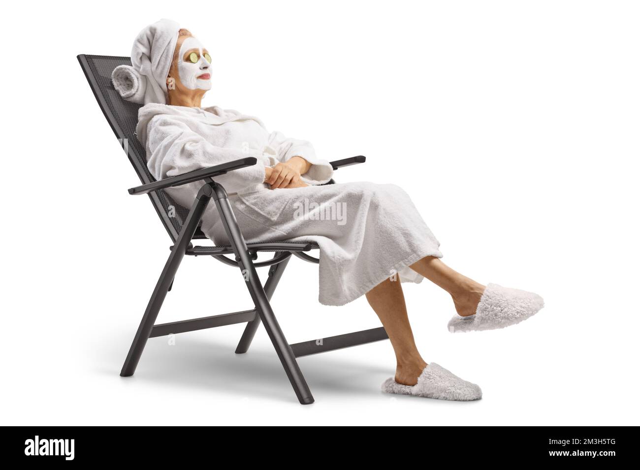 Woman in a bathrobe with a face mask sitting on a chair with cucumber ...