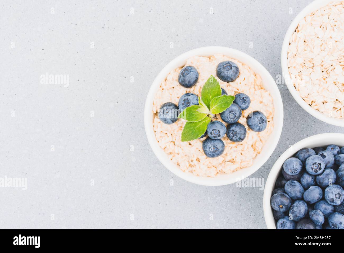 White bowls with oatmeal porridge and organic fresh blueberry on light ...