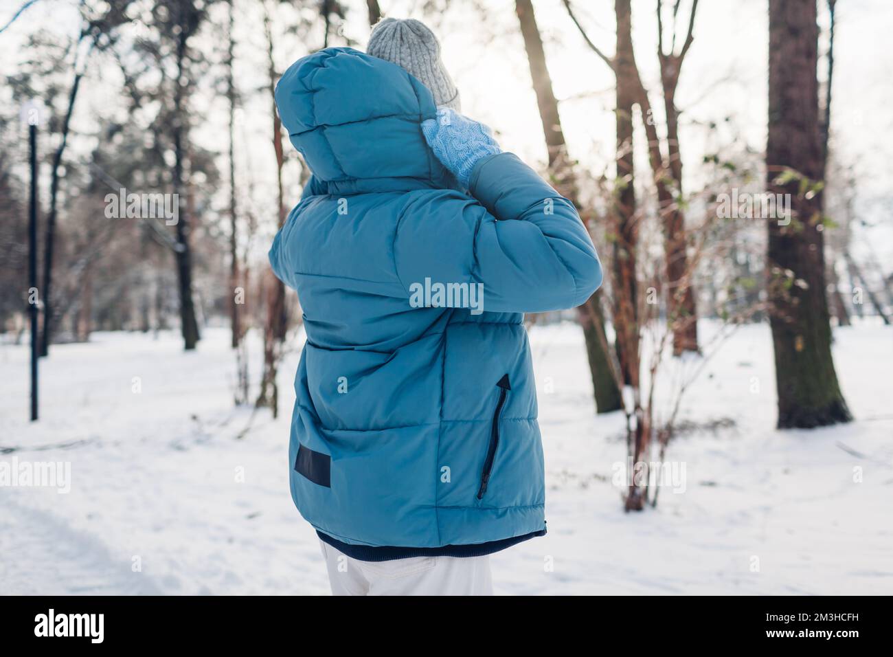 Back view of woman walking in snowy winter park wearing blue down ...