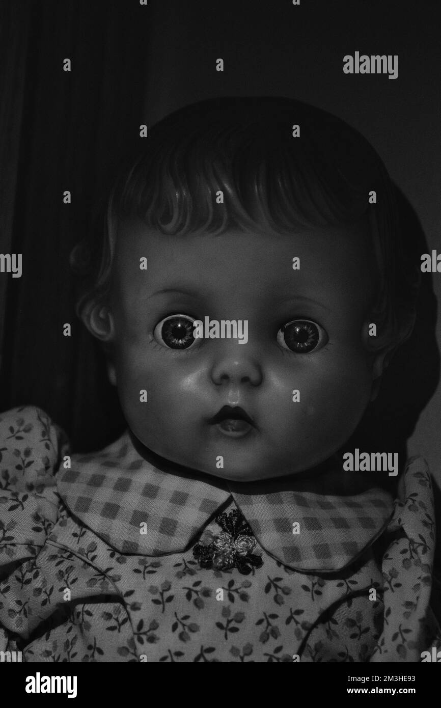 Antique doll in dark room with big eyes wearing a dress with flowers ...