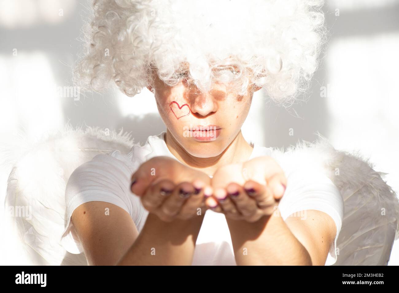 A young girl in an angel costume with wings and curly hair stretched ...