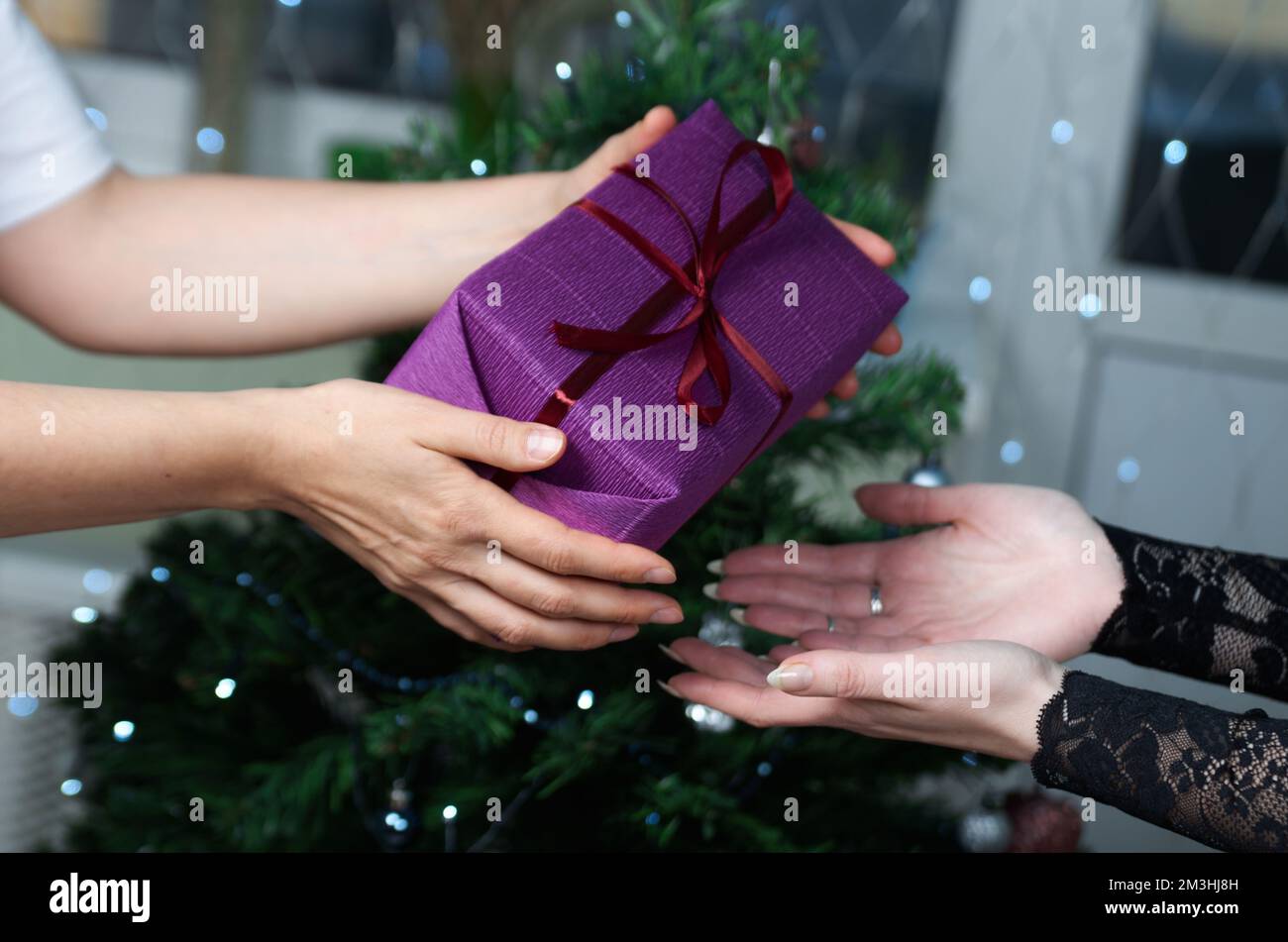 Close-up of the hands of two women passing a Christmas present to each ...
