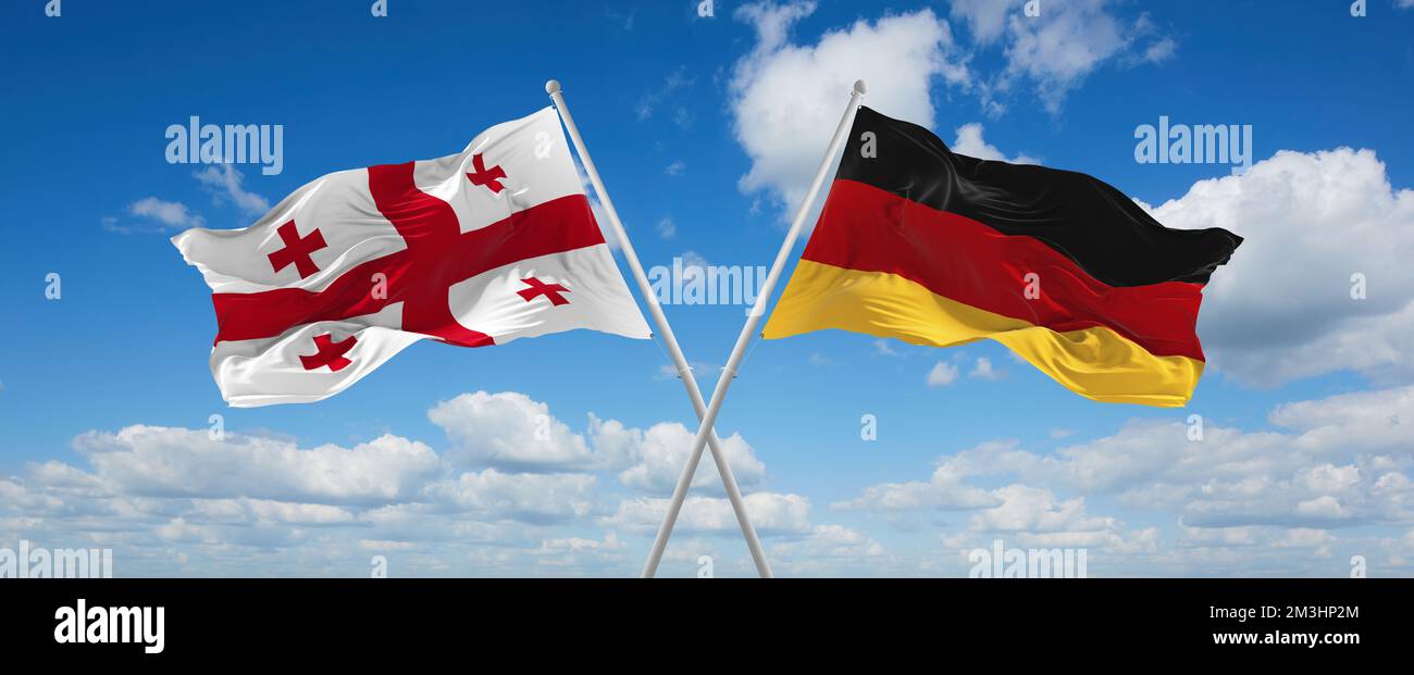 two crossed flags Federal Republic of Germany and Georgia waving in wind at cloudy sky. Concept ...