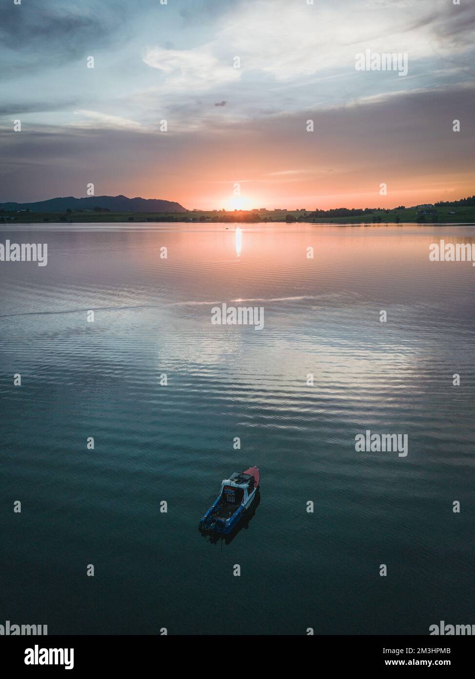 A drone vertical shot of a boat in a lake with cloudy sky at sunset ...