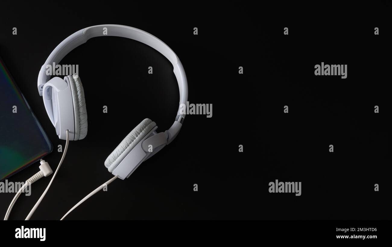 White headphones and part of smartphone on a black background ...