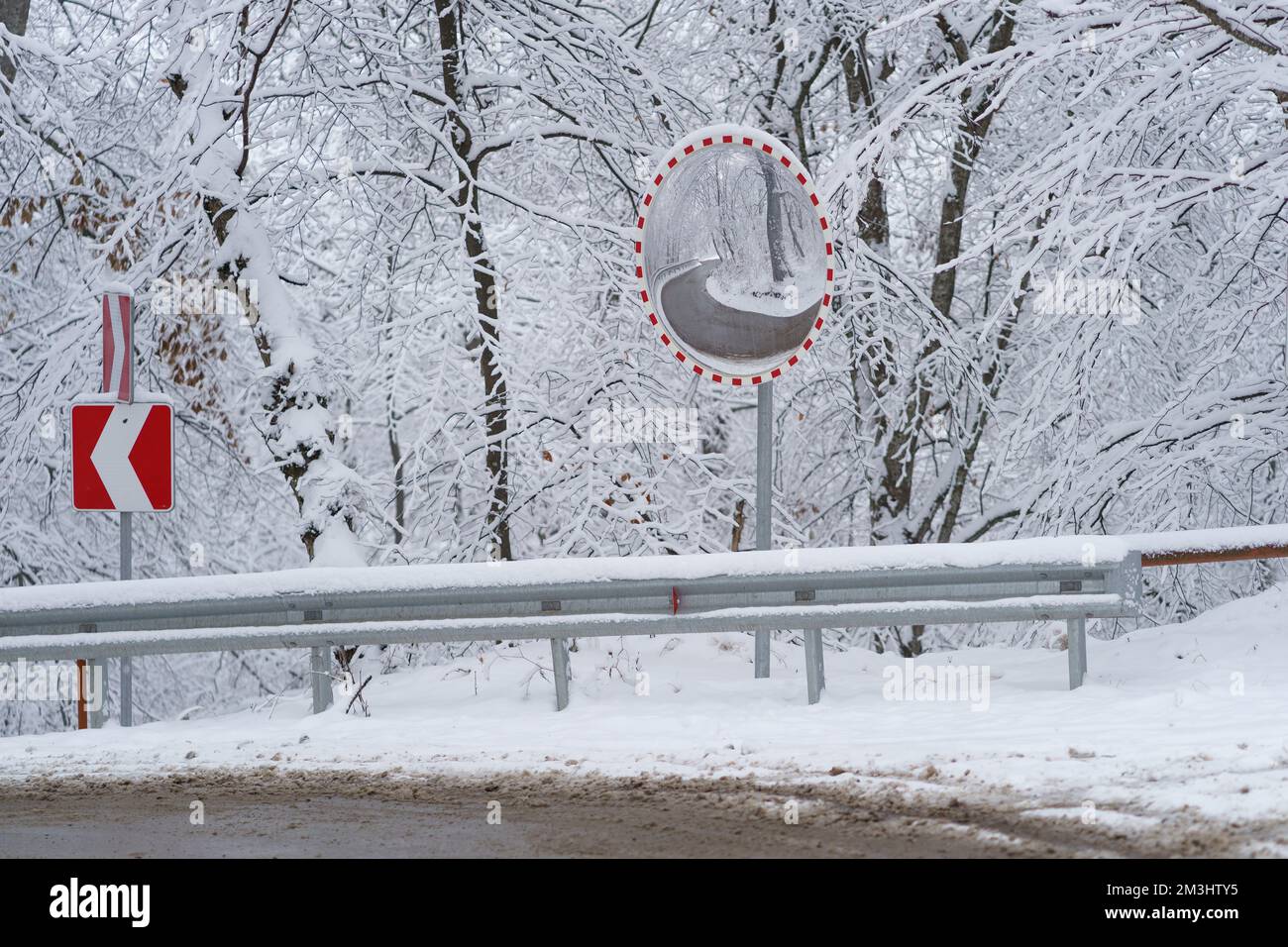 Winter road with mirror installed near sharp turn fenced with iron bump ...