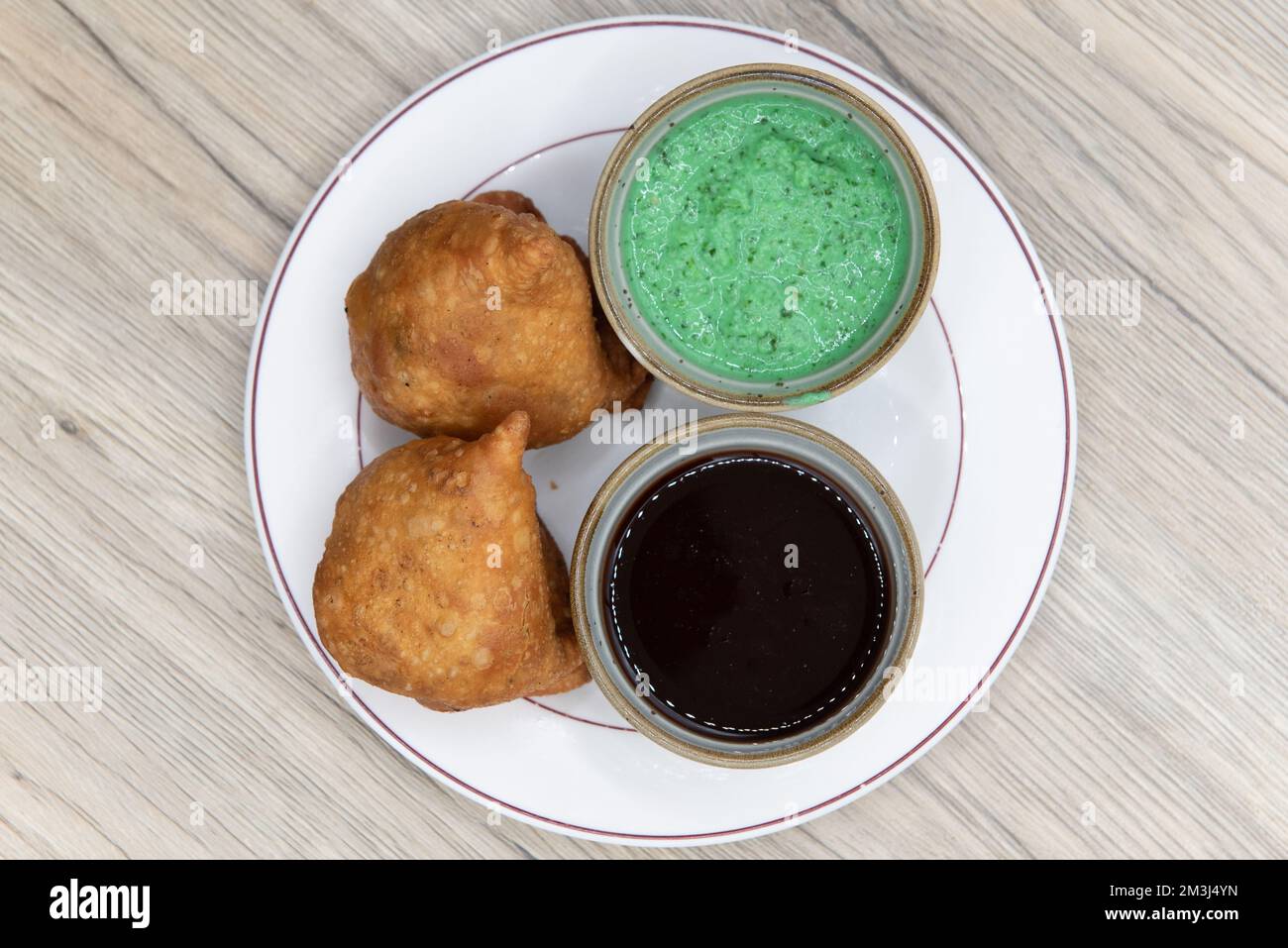 Overhead view of crispy samosa pair on a plate with humus cipping sauce ...