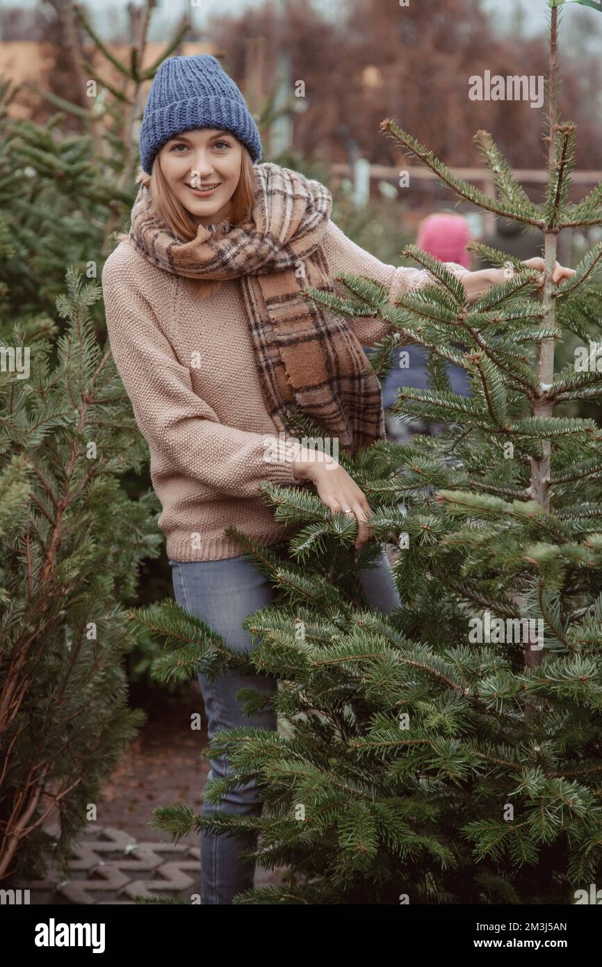 Elegant girl buys a Christmas tree. Womanin a blue cap and scarf ...