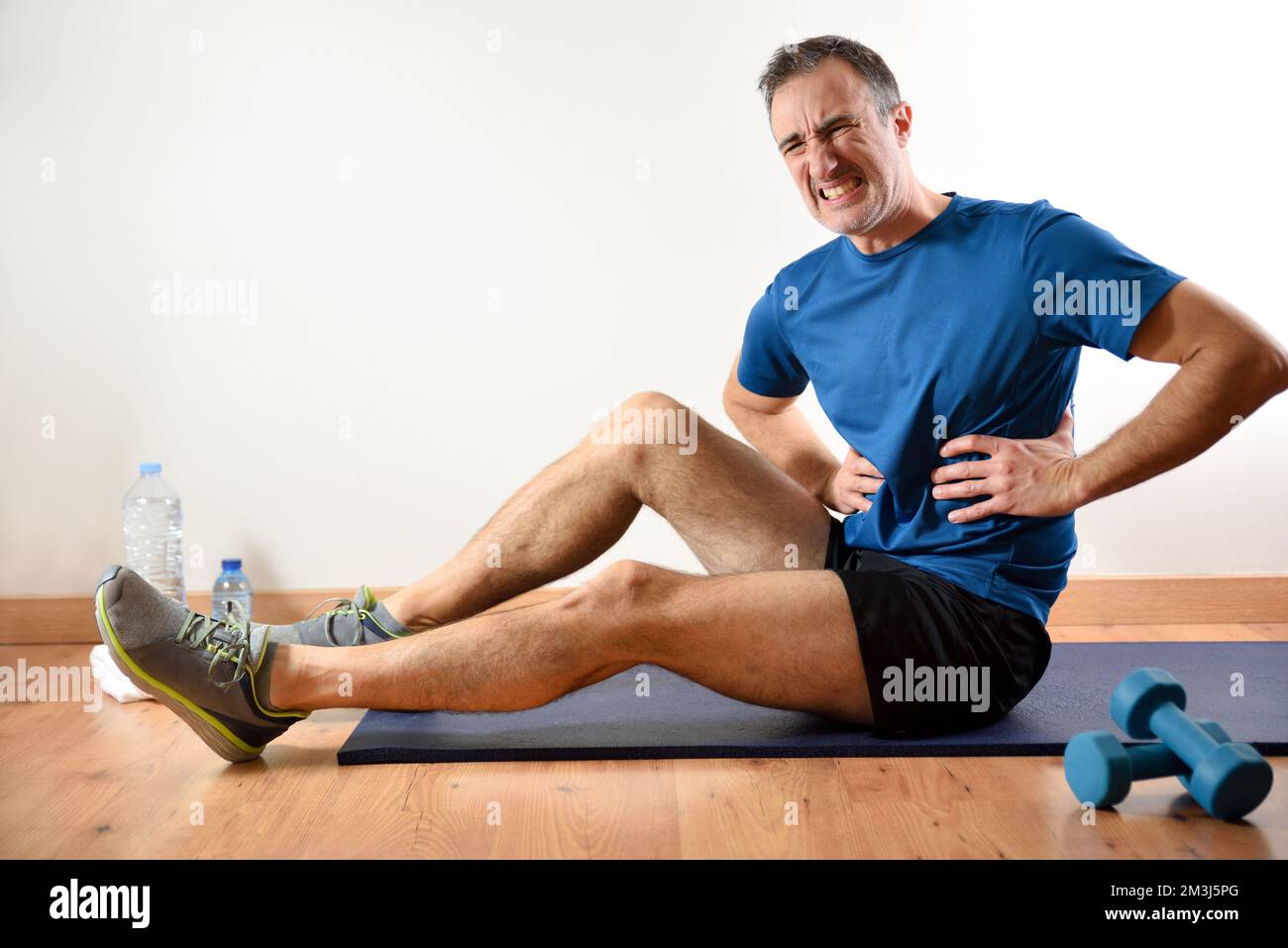 Man doing sports indoors complaining of ribs pain sitting on a mat ...