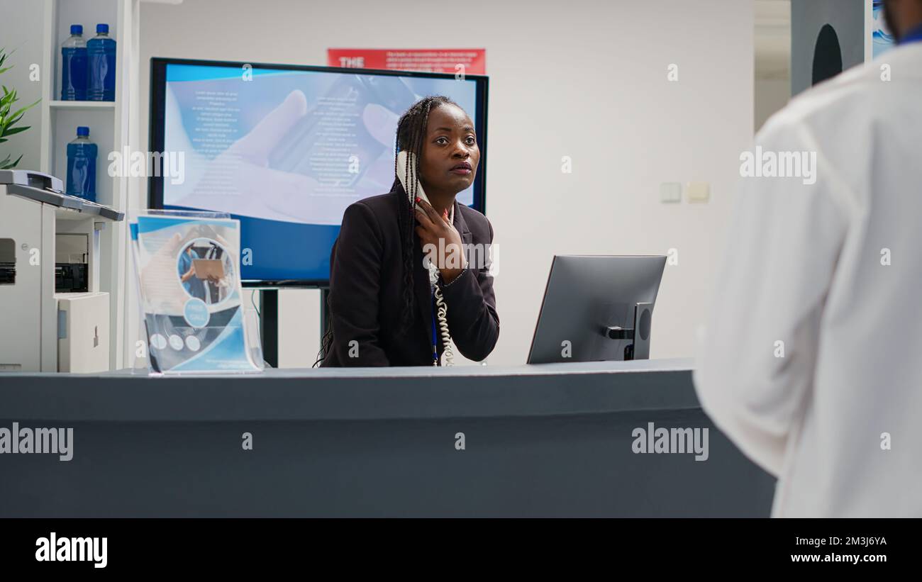 African american woman answering landline phone call at reception ...
