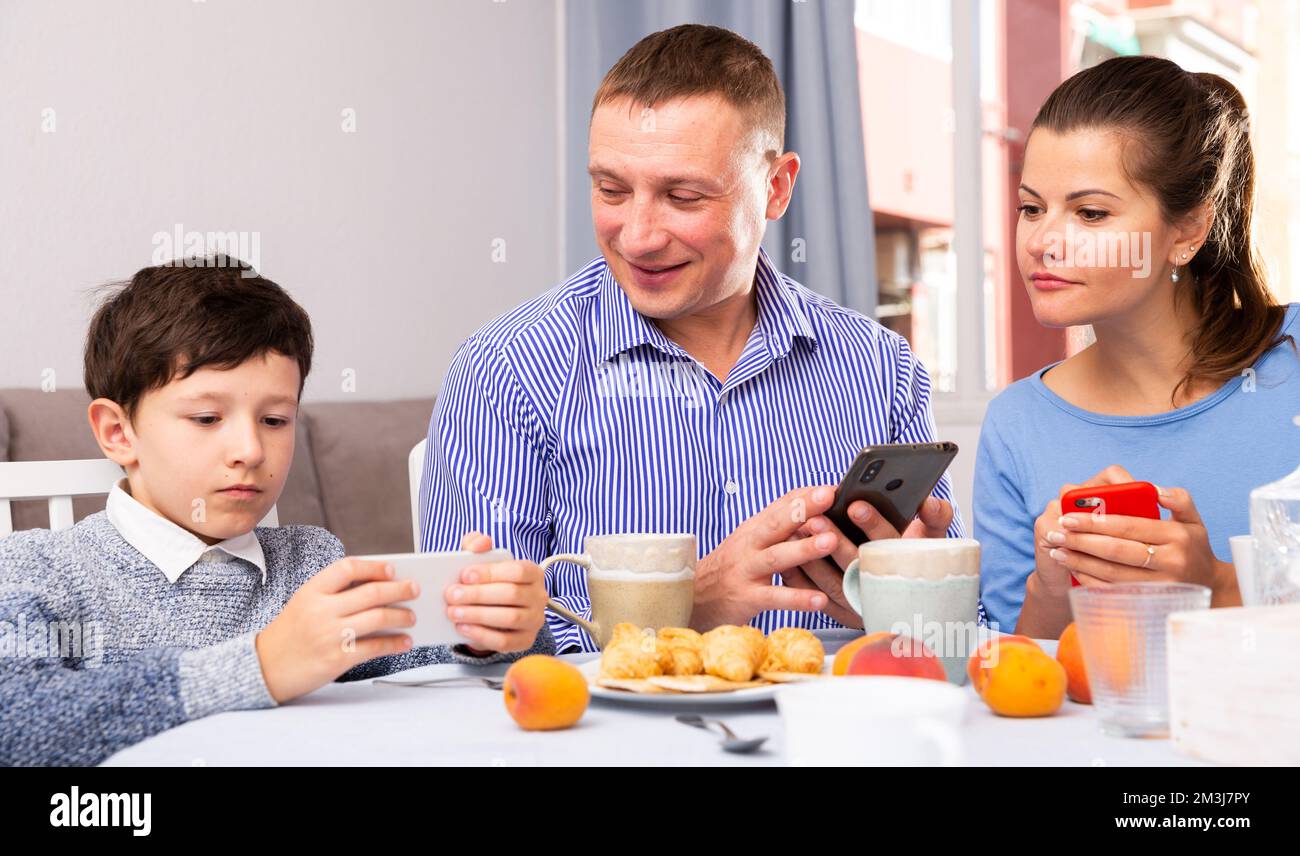 Parents and teen son using phones at kitchen Stock Photo - Alamy