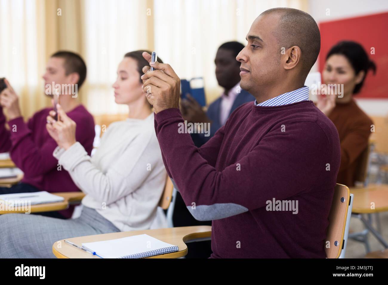 Students of different age sitting together at tables, shooting lesson ...