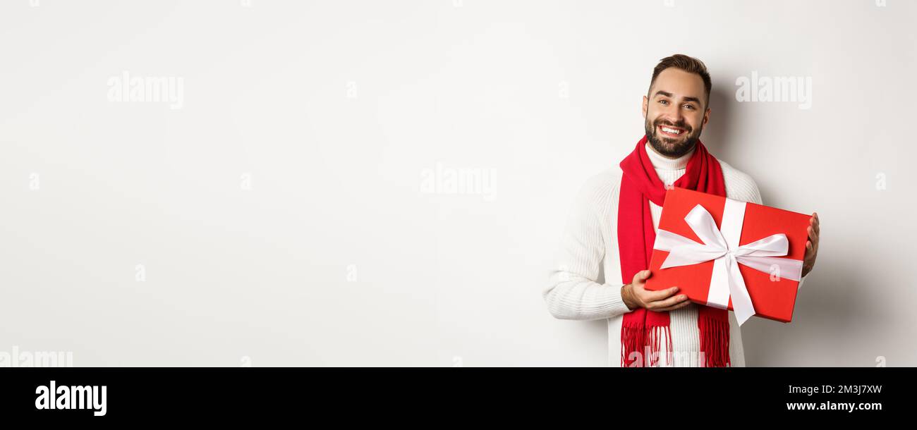 Christmas. Handsome young man holding gift and smiling, wishing happy ...