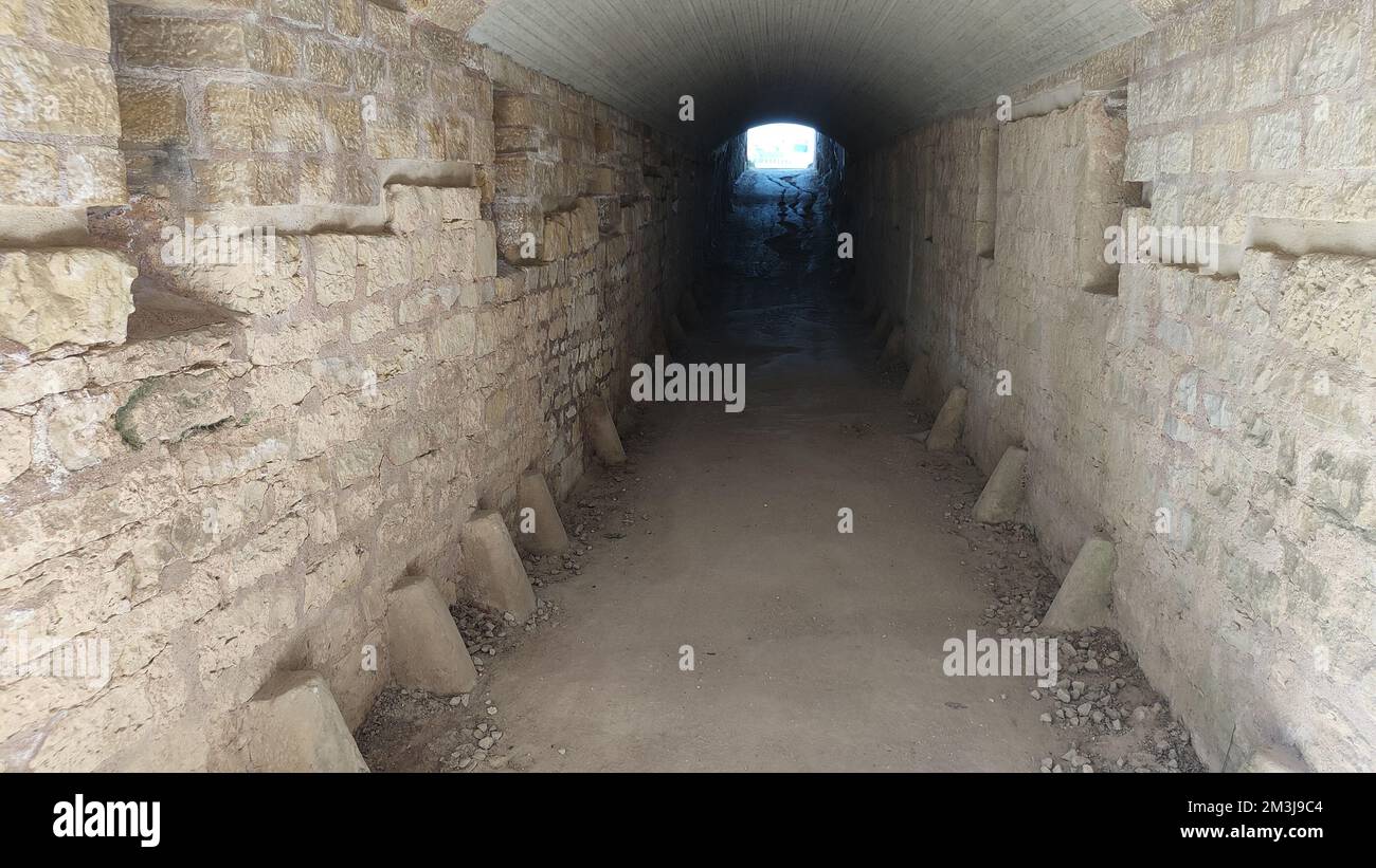 A tunnel path surrounded by stone walls leading to a light Stock Photo ...