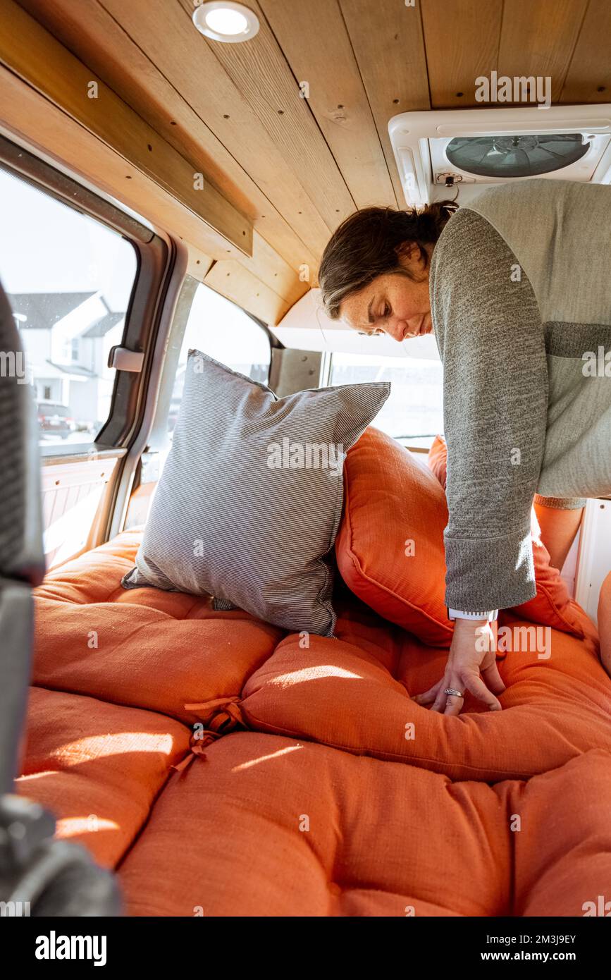Young 30s caucasian woman with dark hair making the bed in a self ...