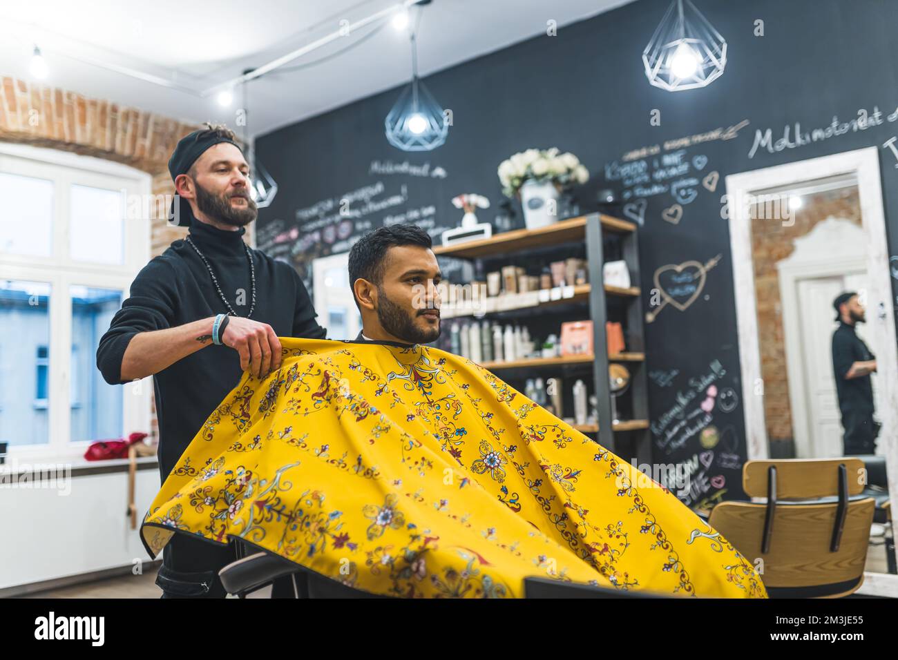 Professional male barber putting on yellow patterned cape on his ...