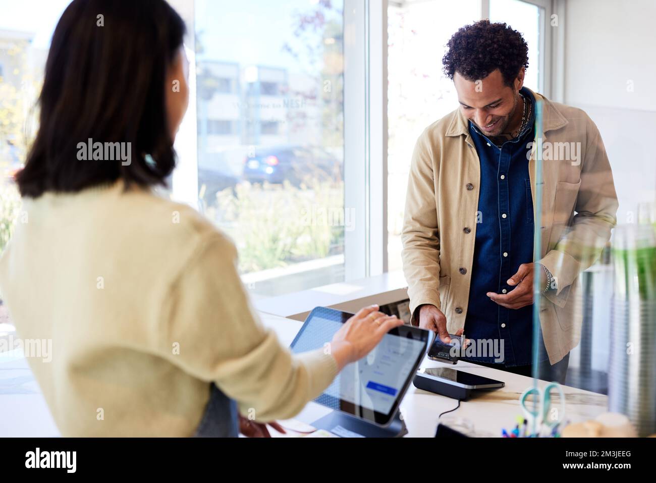 Smiling man paying through smart phone by at checkout counter in cafe ...
