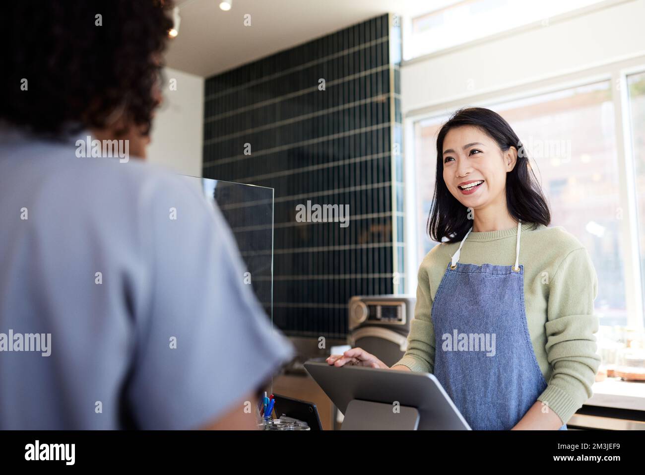 Smiling cafe owner with apron talking to customer at checkout counter ...