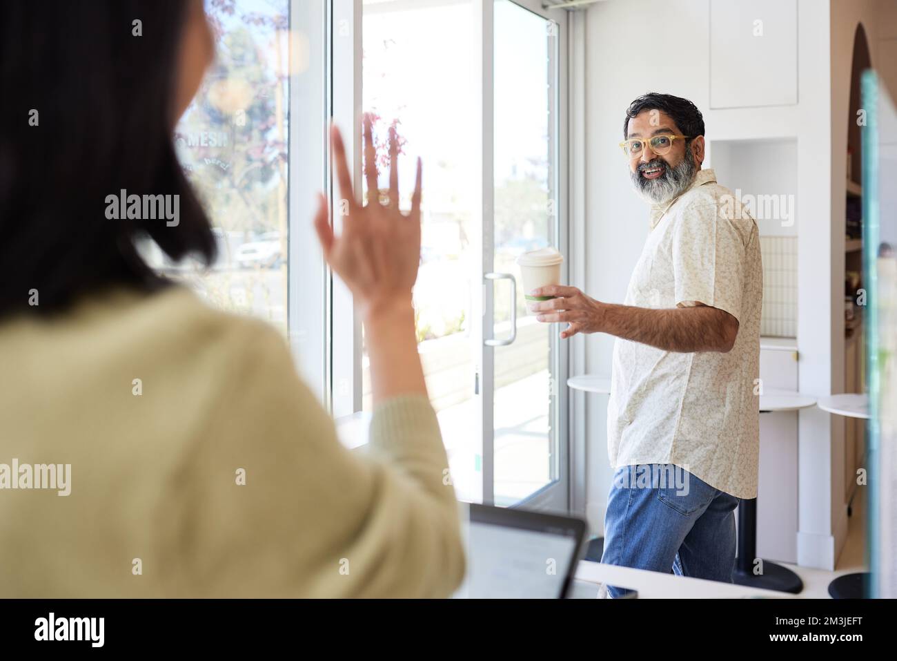 Female owner waving at smiling male customer leaving cafe Stock Photo ...