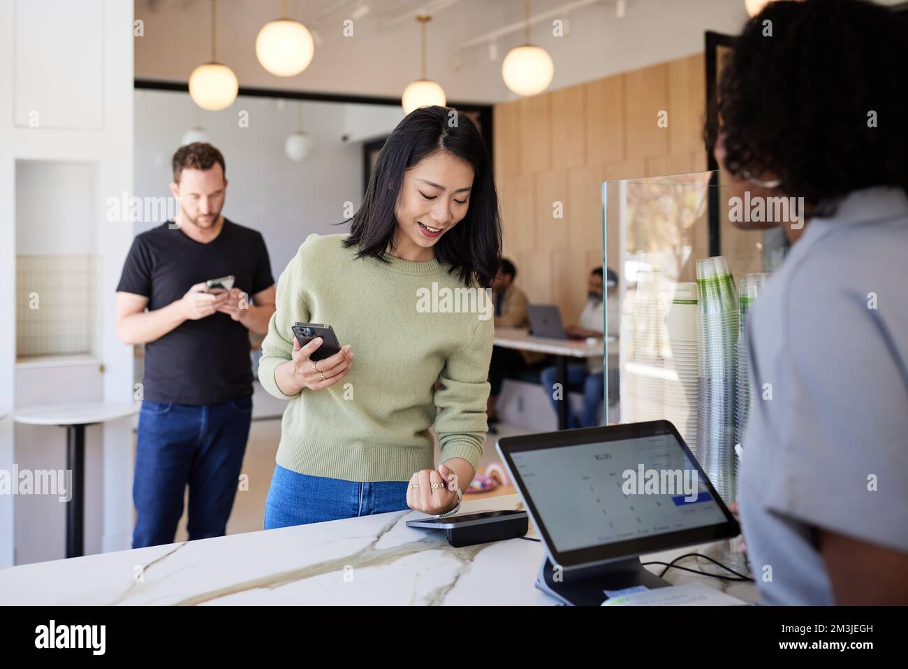 Smiling woman paying through smart watch at POS system on counter Stock ...