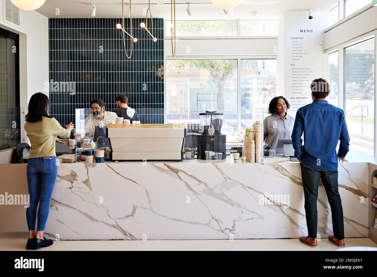Rear view of customers talking with staff at counter in coffee shop ...