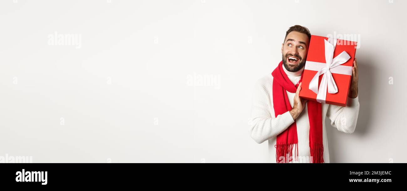 Concept of winter holidays. Happy man shaking gift box to guess what ...