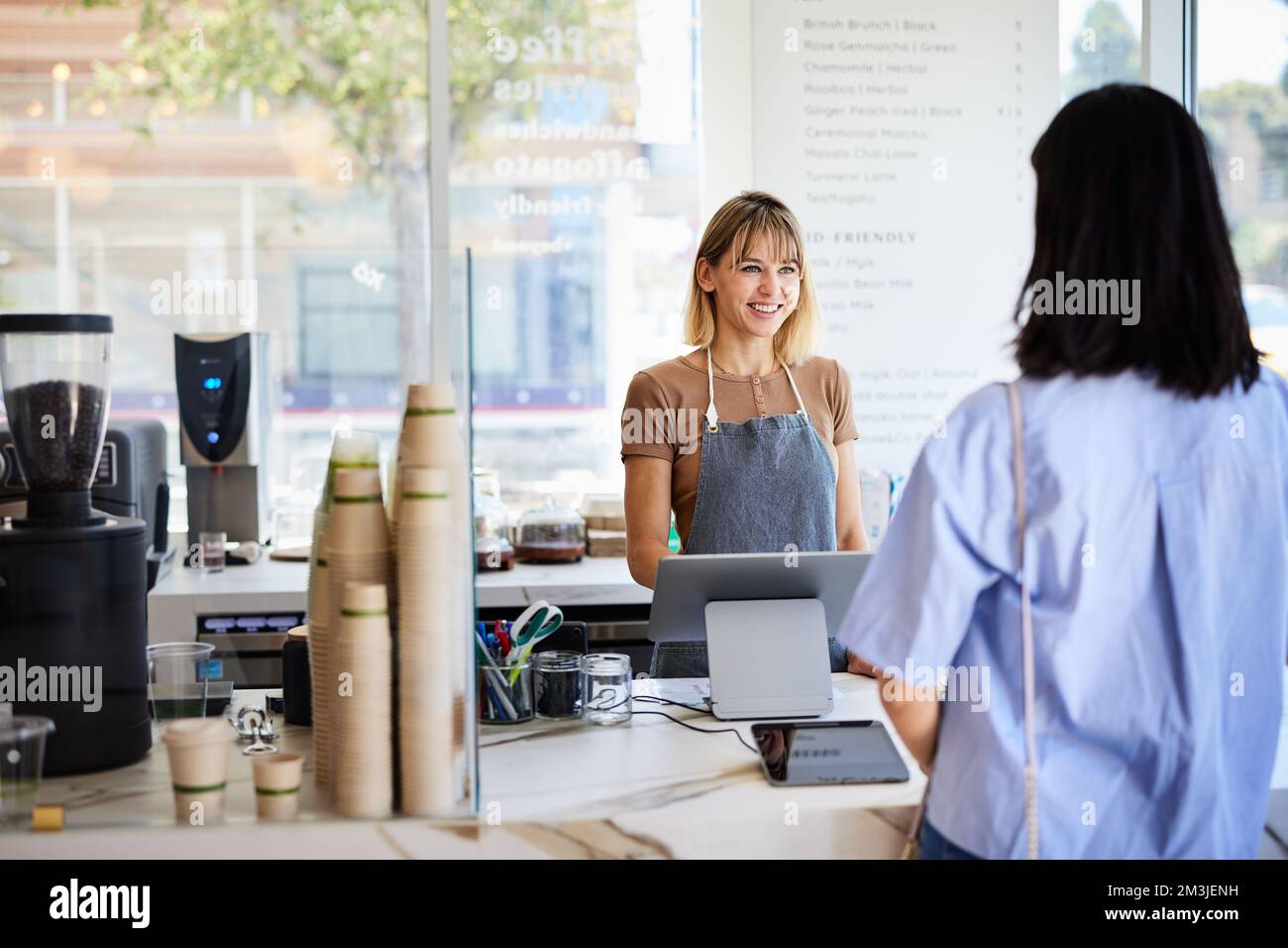 Smiling owner talking to female customer at checkout counter Stock ...
