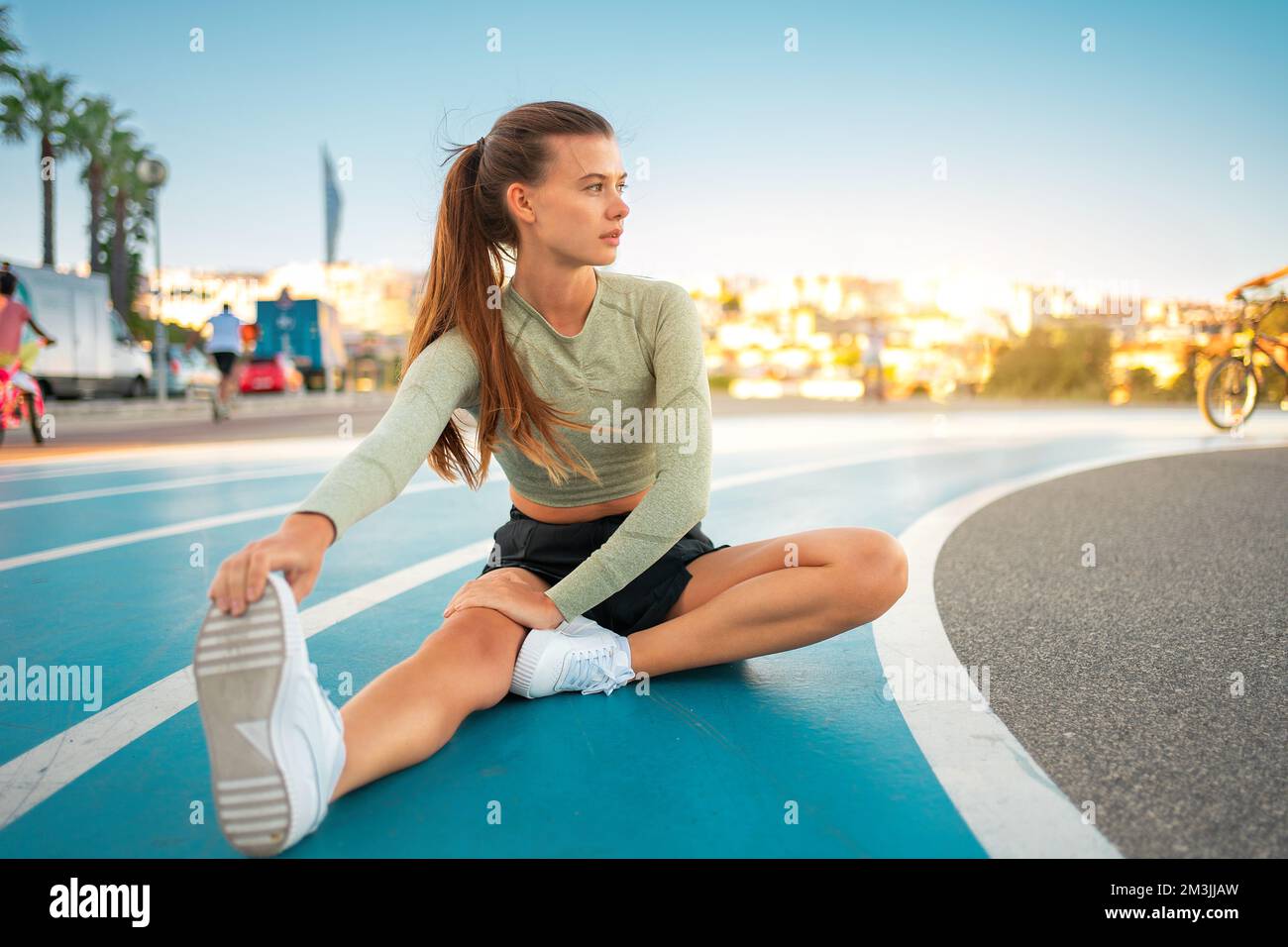 Sportswoman sitting and stretching on blue track field. Woman runner ...
