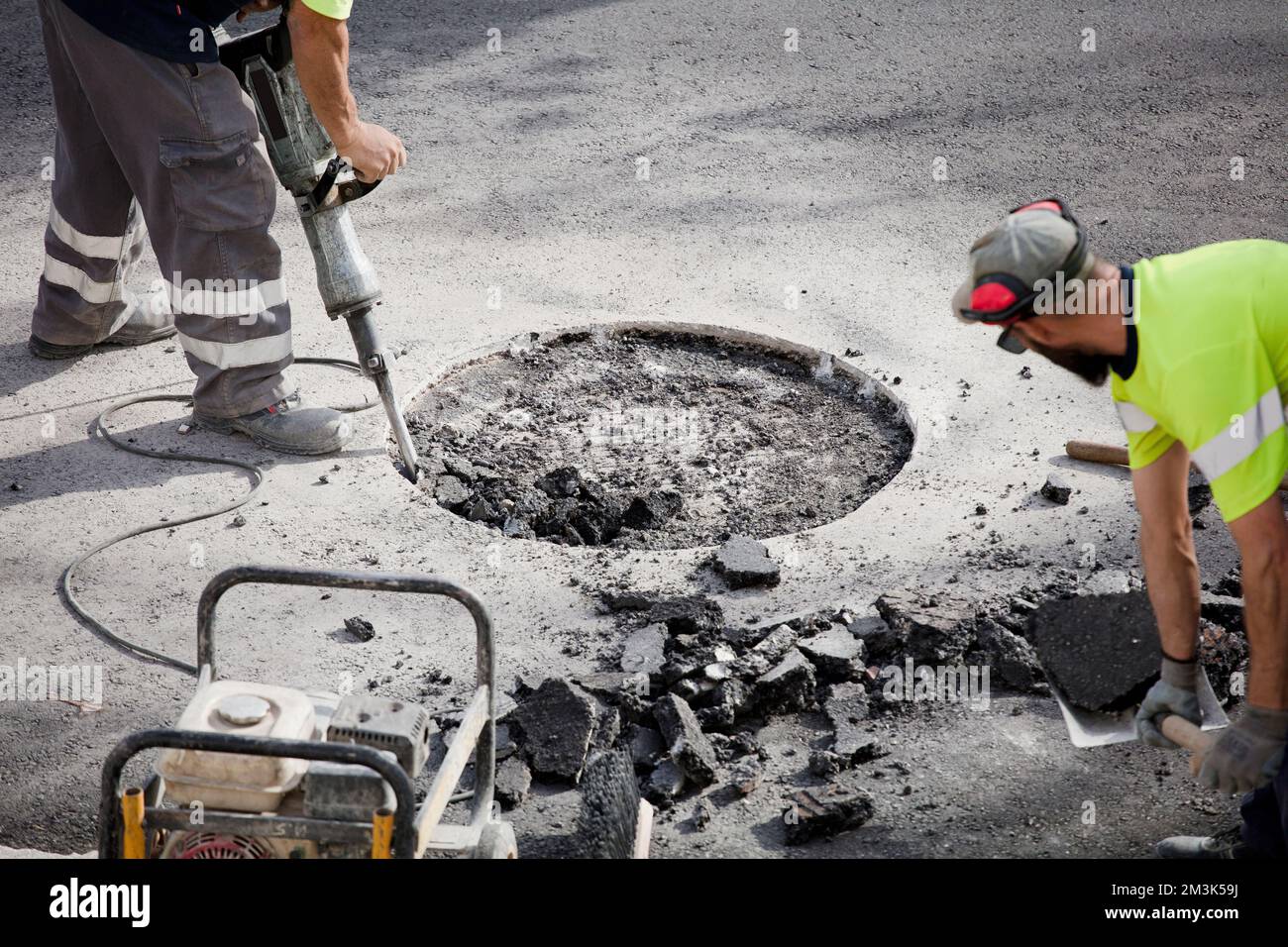 hydraulic hammer in the hands of an operator in uniform works the asphalt, partner collects ...