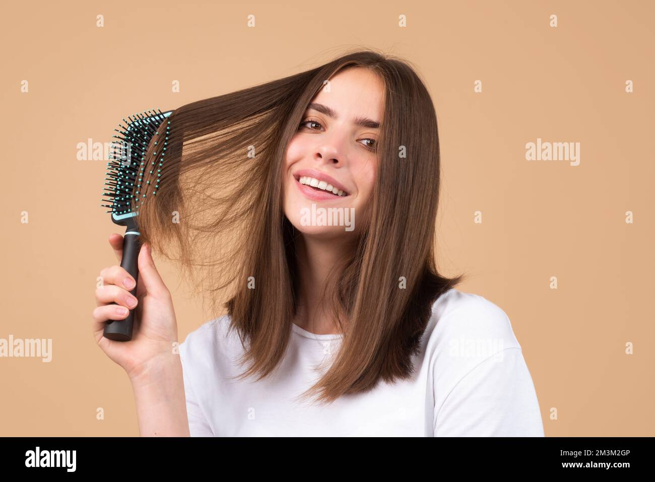 Young woman combing healthy and natural shiny hair, isolated on studio ...