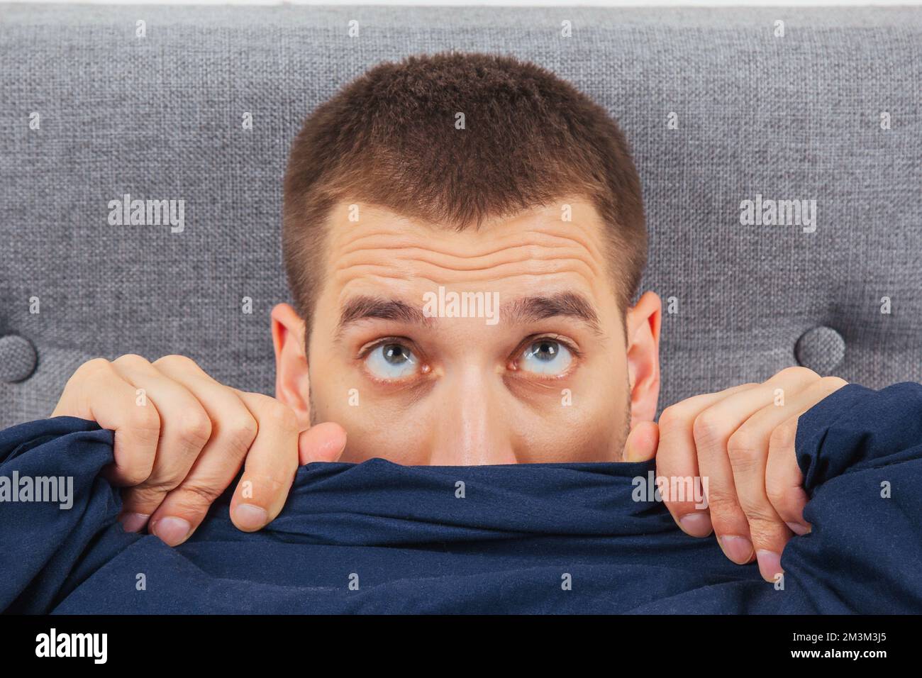 Look up. A handsome young guy hiding behind a blanket looks to the side ...