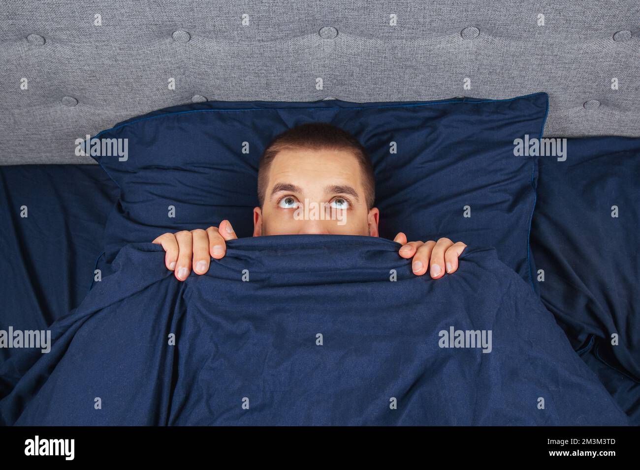 Look up. A handsome young guy hiding behind a blanket looks to the side ...