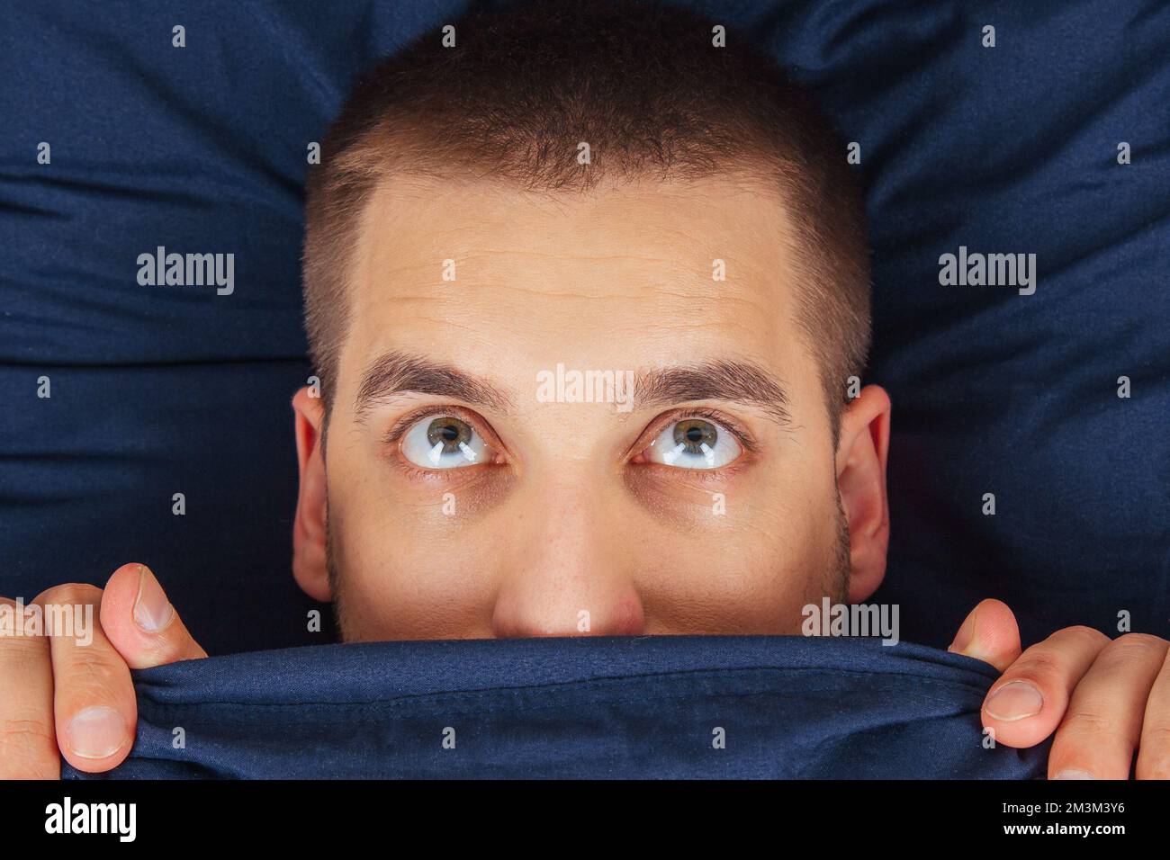 Look up. A handsome young guy hiding behind a blanket looks to the side ...