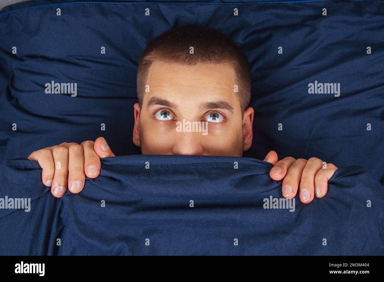 Look up. A handsome young guy hiding behind a blanket looks to the side ...